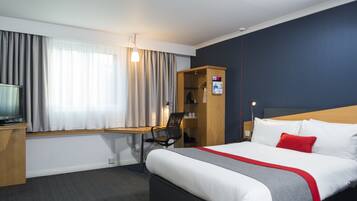 Quarto de hotel com cama, escrivaninha, cadeira, televisão e armário.