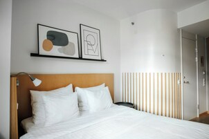 Cama bem arrumada com lençóis brancos, cabeceira de madeira e duas obras de arte abstrata emolduradas na parede acima.