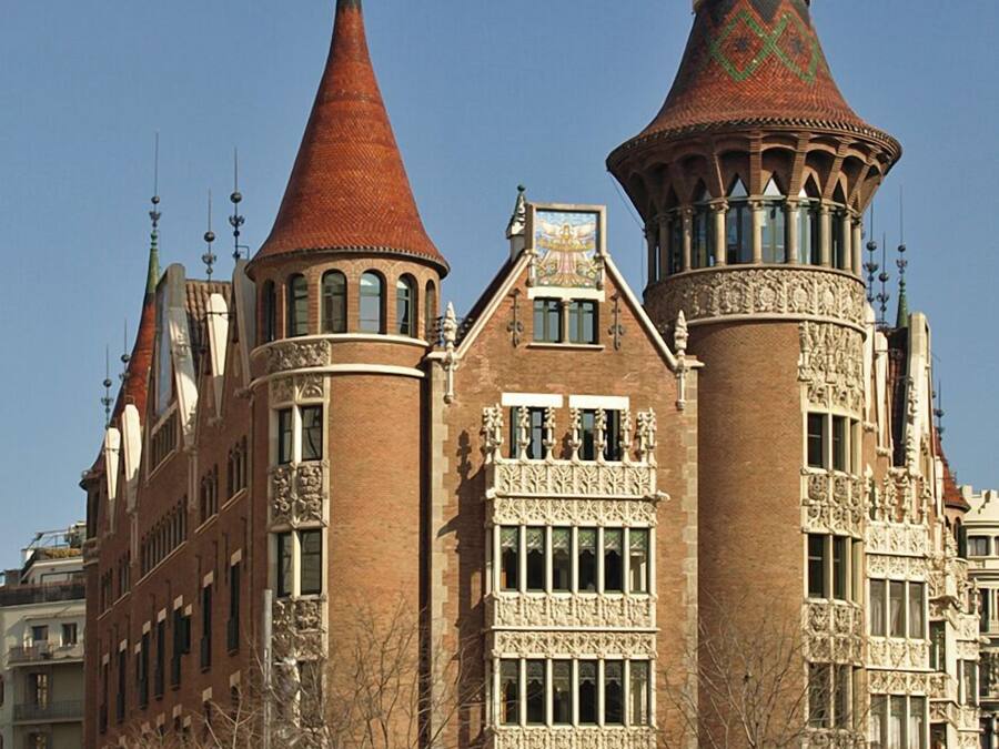 Um edifício histórico com duas torres notáveis, uma com telhado cónico e outra com pináculo.