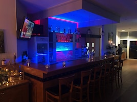 Uma área de bar moderna com balcão, assentos e uma tela de televisão.