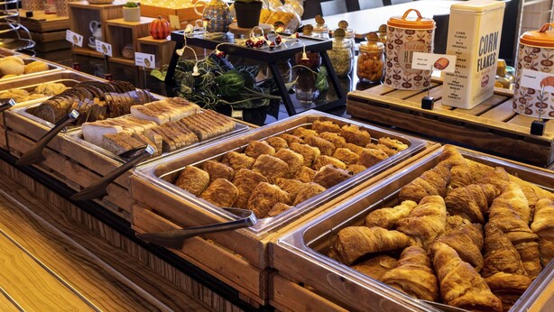 Buffet com diversos alimentos, incluindo pão, doces e um arranjo floral.