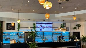 Uma área de bar com assentos, uma tela de televisão e diversos frascos em prateleiras.
