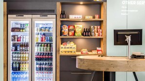 Quarto de hotel com minibar, um aviso 'TAKE AWAY', uma mesa de madeira e uma televisão presa à parede.