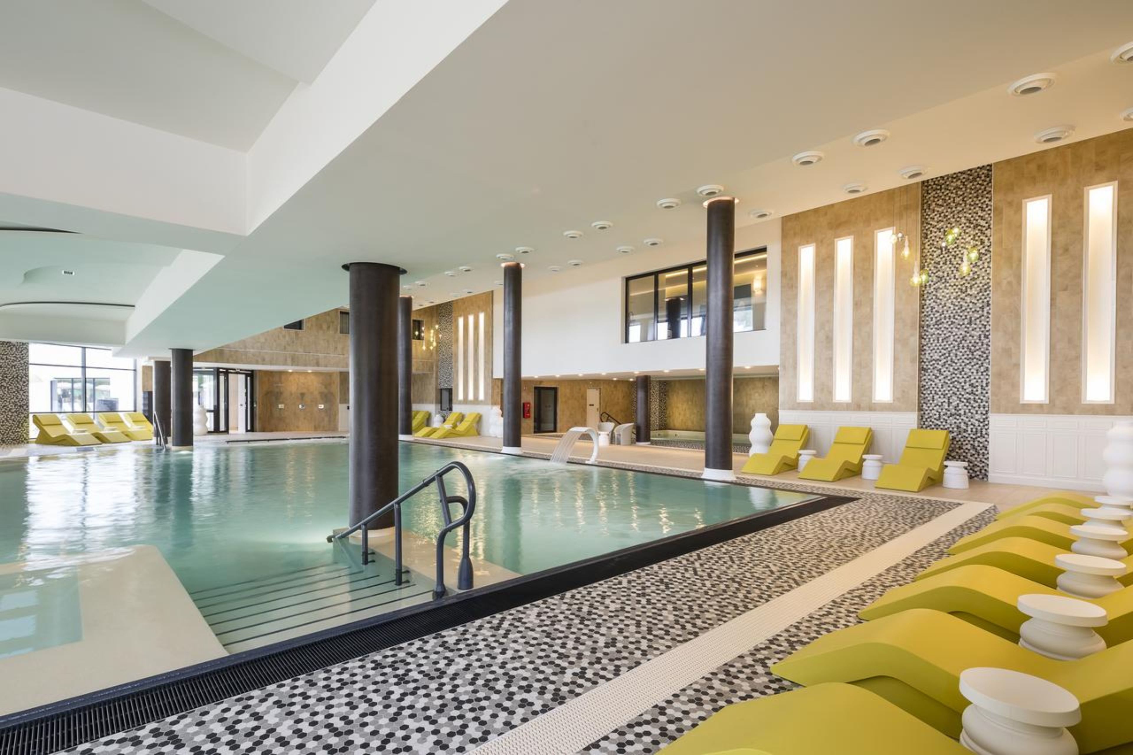 Uma grande piscina interior com cadeiras de descanso amarelas e chão revestido de azulejos.
