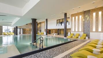 Uma grande piscina interior com cadeiras de descanso amarelas e chão revestido de azulejos.