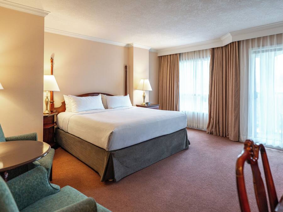 Quarto de hotel com uma cama, duas mesas de cabeceira com luminárias, uma cadeira e uma mesinha.