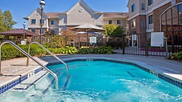Piscina com escada de metal, cercada por uma grade, e um edifício com fachada de pedra ao fundo.