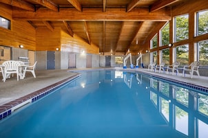 Piscina interna com água azul cristalina, rodeada por paredes de madeira e grandes janelas.