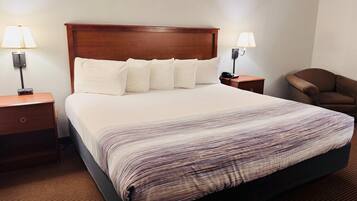 Quarto de hotel com uma cama grande, duas mesas de cabeceira com abajures, uma cadeira e uma cabeceira de madeira.