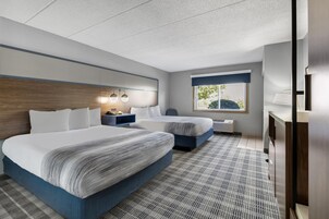 Quarto de hotel com uma cama grande, uma cama menor, escrivaninha, cadeira, janela com vista e televisão de tela plana.