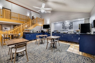 Cozinha espaçosa com escada de madeira, área de jantar com mesa e cadeiras, e ilha central com geladeira.