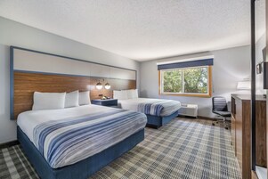 Quarto de hotel com uma cama grande, duas mesas de cabeceira, uma escrivaninha e uma janela com vista para árvores.