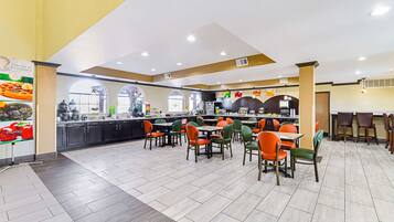 Um restaurante espaçoso com várias mesas e cadeiras, uma área de cozinha e janelas amplas.