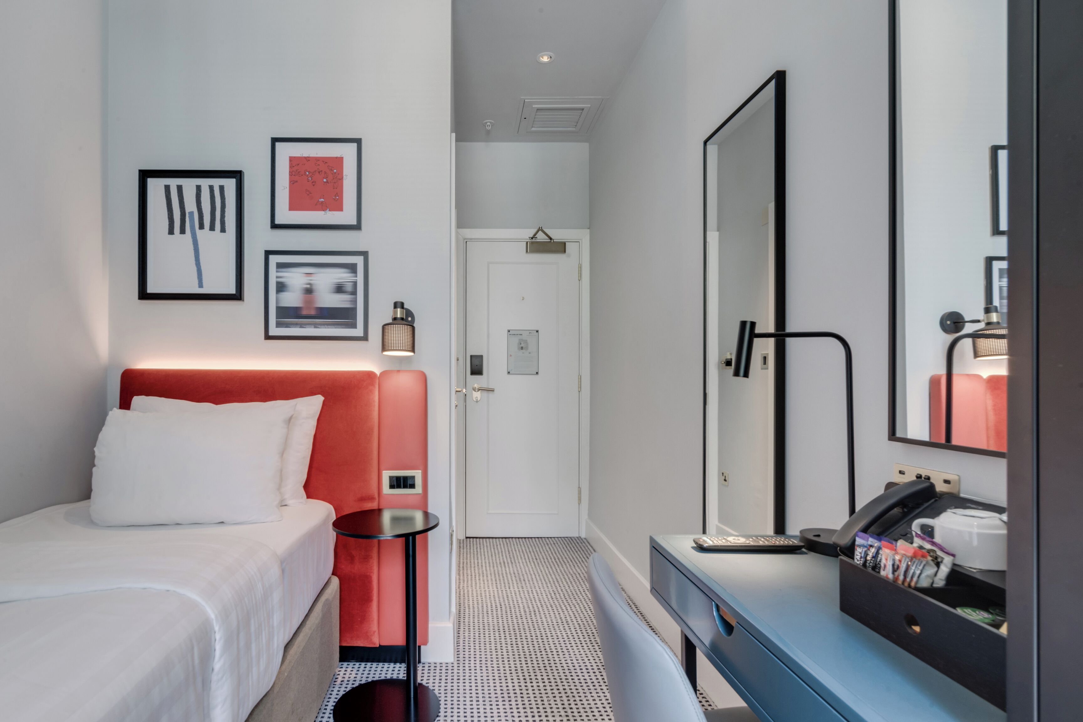 Quarto de hotel com cama, escrivaninha, cadeira, espelho e obras de arte na parede.