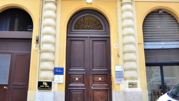 Um edifício amarelo com uma grande porta de madeira, duas janelas com persianas e uma placa do Hotel Adler.