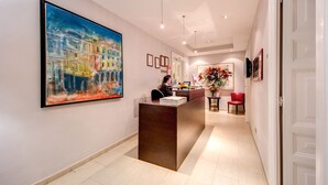 Uma área de recepção de hotel com uma pintura grande, um balcão de recepção e uma cadeira vermelha.