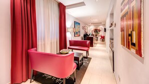 Uma sala de estar moderna com cadeiras vermelhas, uma mesa de centro e um sofá. Há uma área de jantar com uma mesa e cadeiras ao fundo.