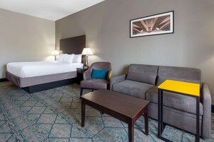 Quarto de hotel com cama, sofá, mesa pequena e mesa de cabeceira com luminárias.