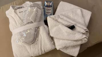 Embalagem contendo um roupão branco, uma garrafa de água mineral Christine Naturelle Carat Naturals e uma toalha branca.