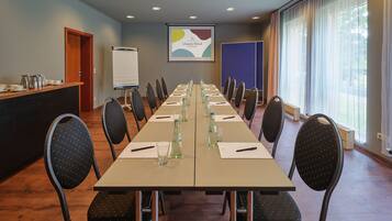 Sala de conferências com uma mesa comprida, cadeiras, tela de projetor e um canto para café.