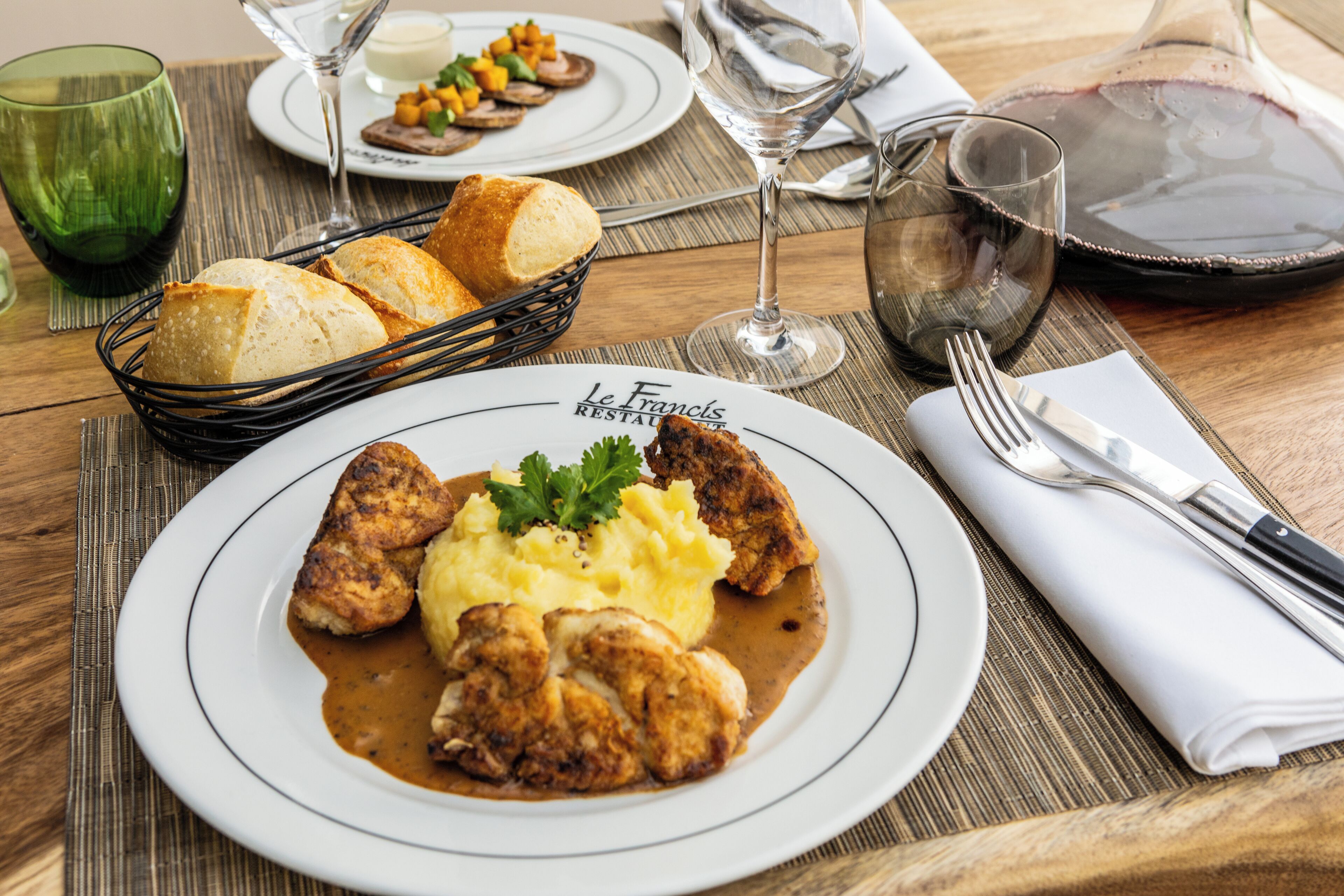 Uma mesa de jantar com um prato de comida, uma cesta de pão e copos de vinho.