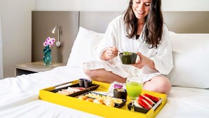 Uma pessoa sentada na cama com uma bandeja de comida e bebida.