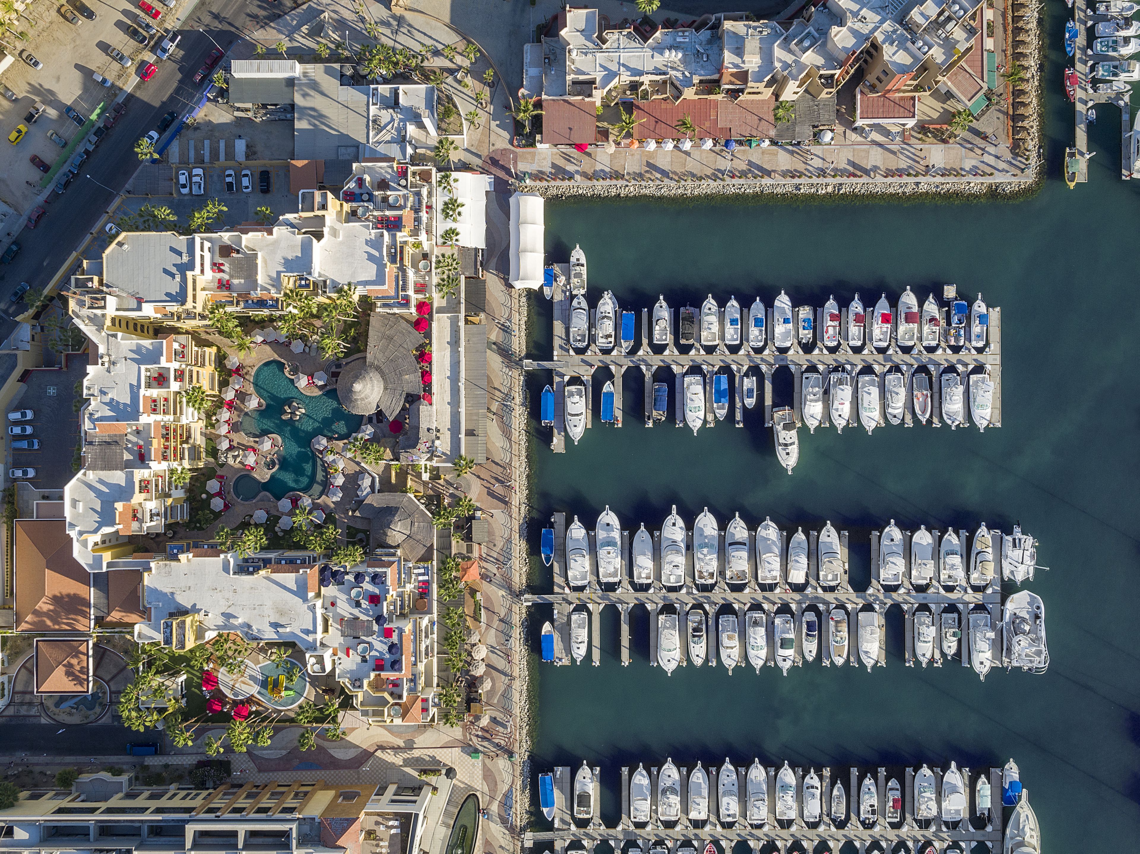 Vista aérea de uma marina com vários barcos atracados, piscina e edifícios próximos com varandas.