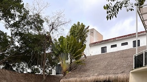Área de piscina com muro de pedra, estrutura com telhado de palha e escadaria que leva a um nível superior.