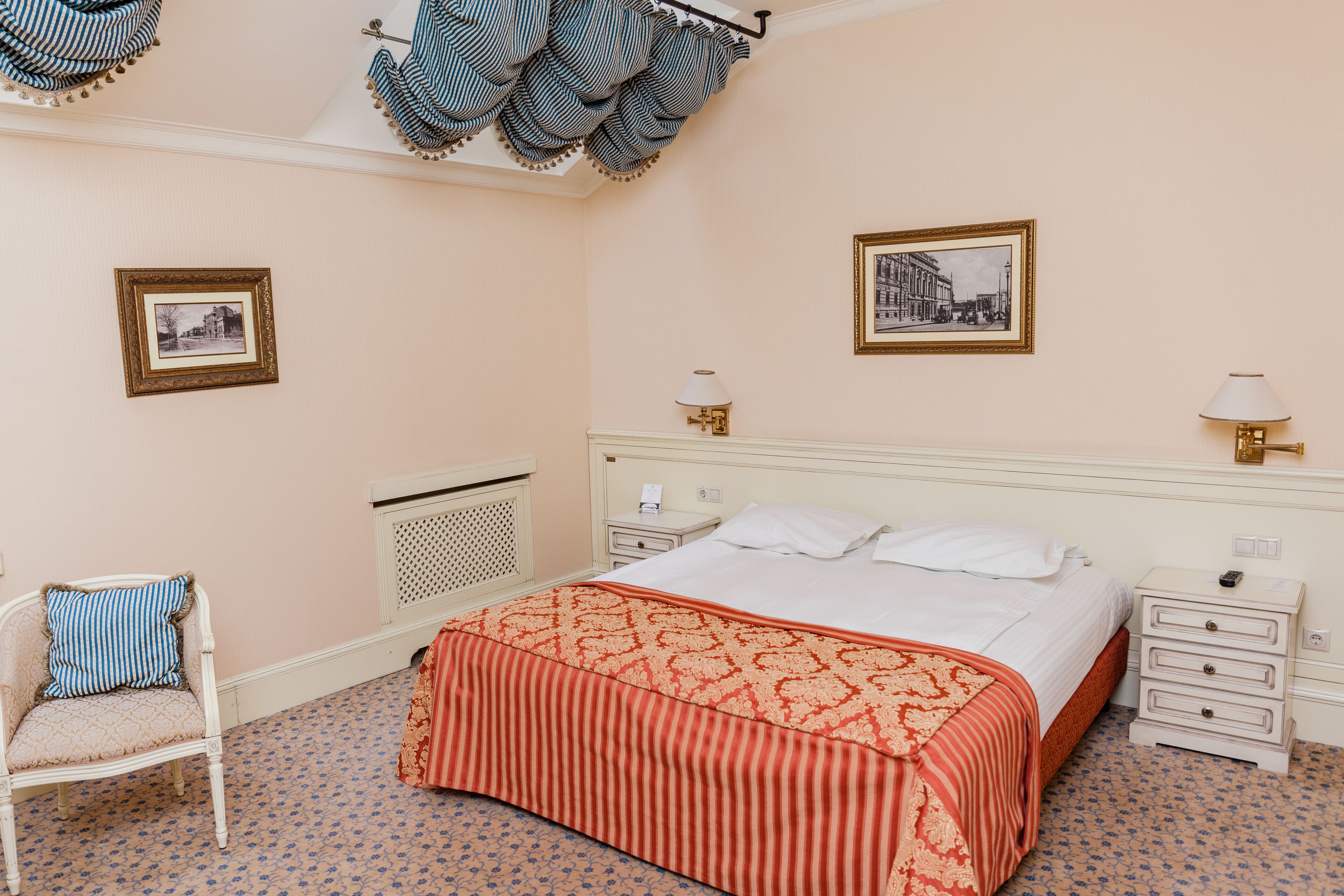 Quarto de hotel com uma cama grande, duas mesas de cabeceira, uma cadeira e duas luminárias na parede.