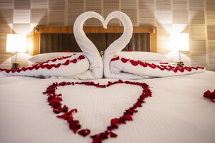 Quarto de hotel com cama, almofadas e decoração em formato de coração feita de pétalas de rosa.