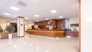 Uma área de recepção de hotel com um balcão de madeira, um relógio e uma máquina de café.