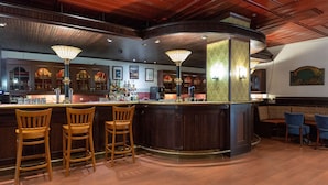 Uma área de bar com banquetas de madeira, balcão curvo e parede estampada.
