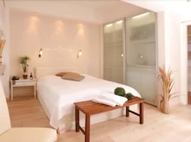 Quarto com cama, mesa de cabeceira e um banco.