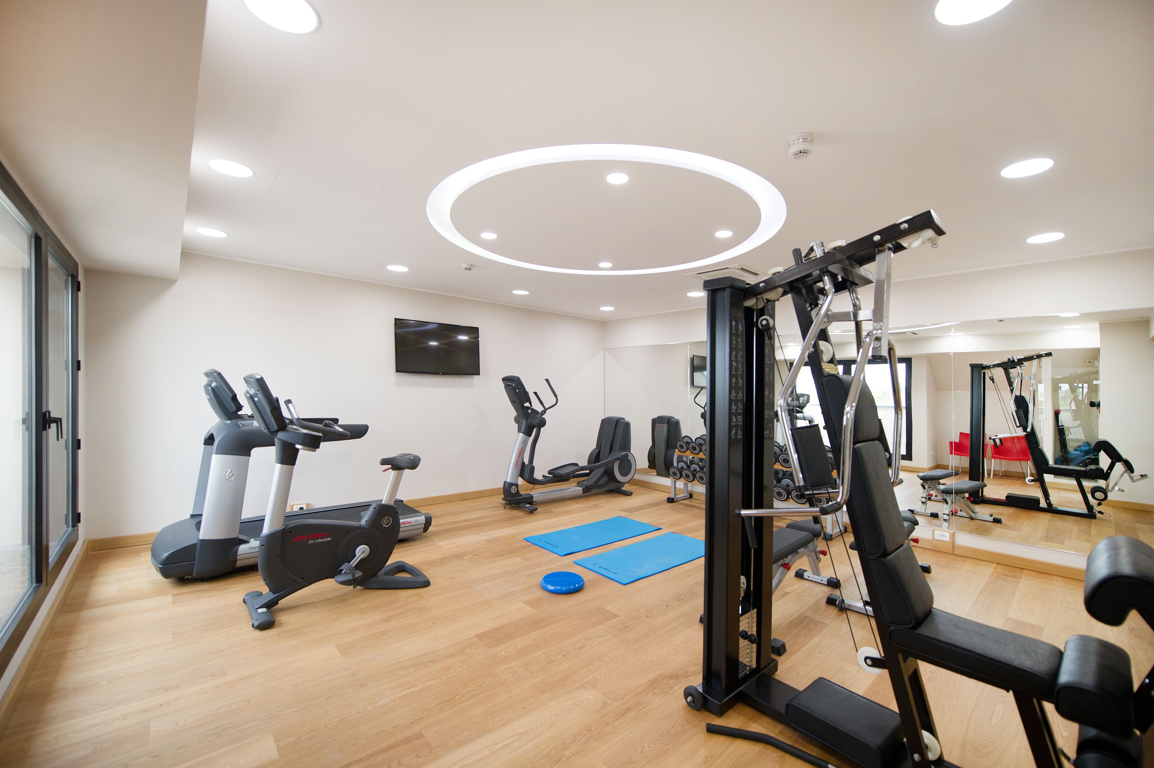 Academia com equipamentos de cardio, pesos livres e um espelho.