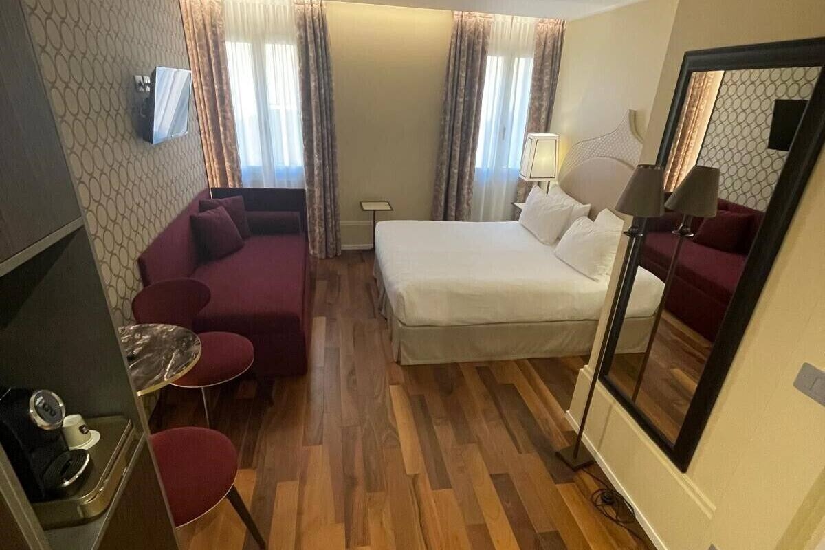 Quarto de hotel com cama, sofá, uma mesinha e um espelho.