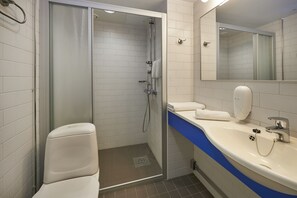 Casa de banho moderna com chuveiro envolto em vidro, sanita branca, lavatório com detalhes em azul e um espelho grande.