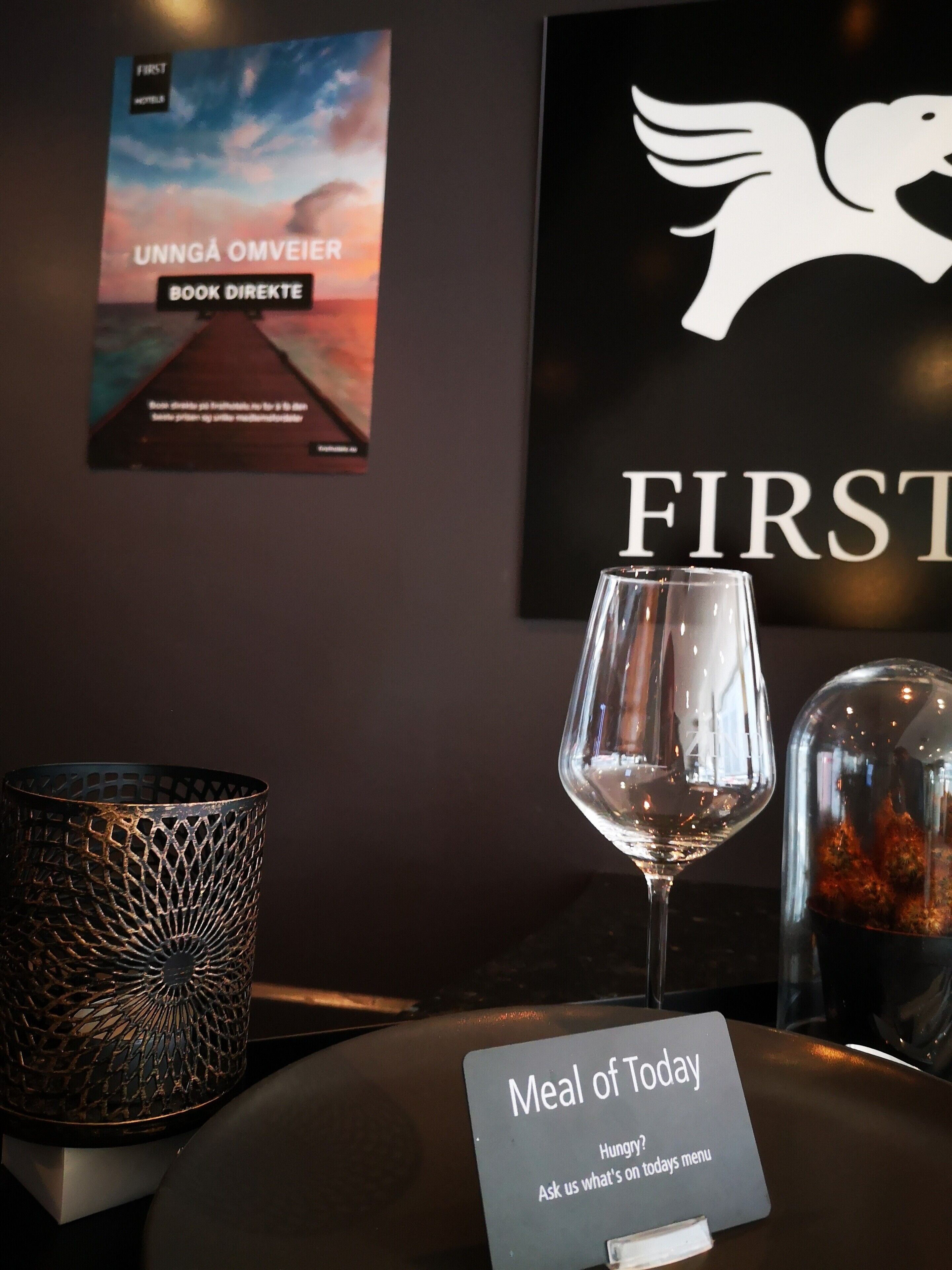 Uma mesa com uma taça de vinho, um letreiro de menu e um livro intitulado 'UNNGA OMVEIER' na parede.