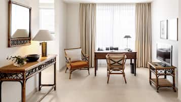 Quarto de hotel com uma mesa de jantar, duas cadeiras, uma TV em um suporte, um abajur e um espelho na parede.