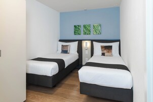 Quarto de hotel com duas camas, parede azul decorativa e uma pequena obra de arte sobre as camas.