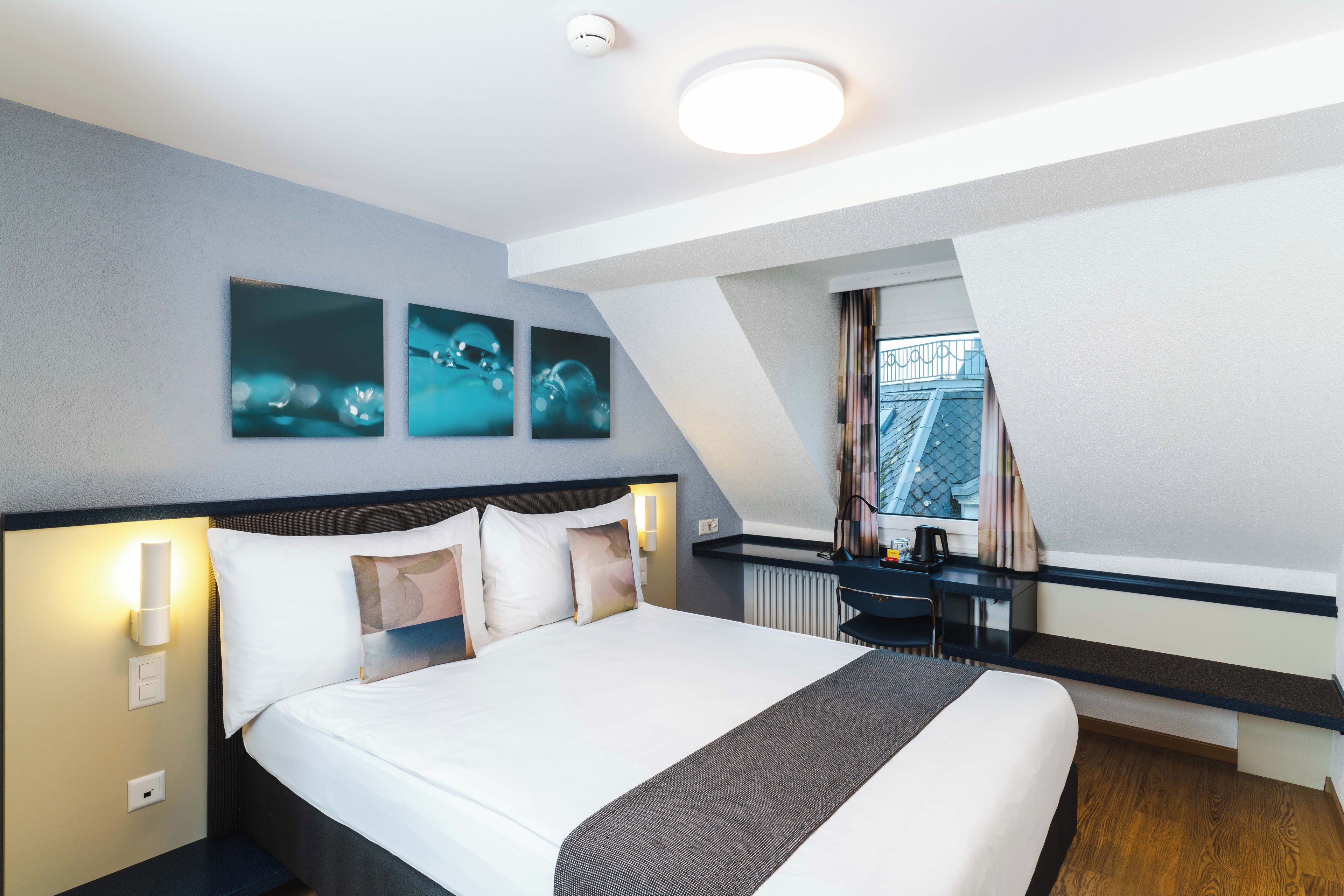 Quarto de hotel moderno com uma cama grande, uma escrivaninha e vista para um edifício através da janela.