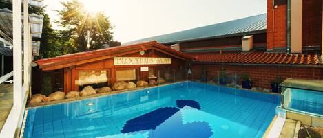 Piscina com área de deck de madeira e uma placa que diz 'Blockhaus Sauna'.