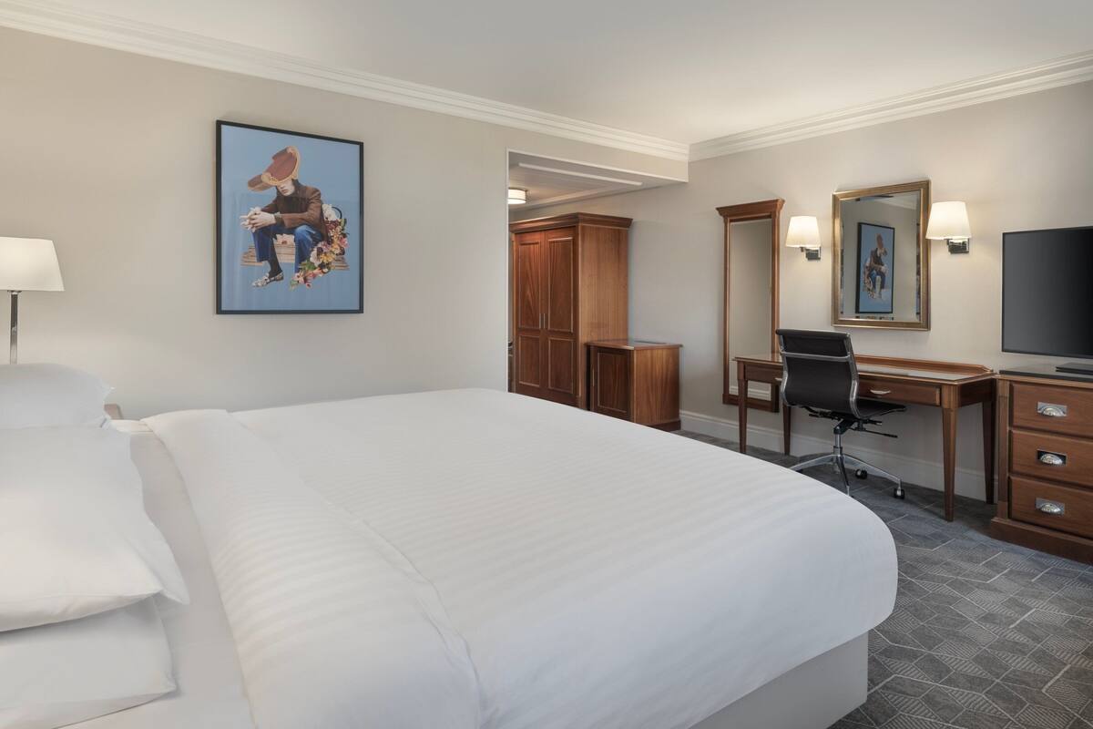 Quarto de hotel com uma cama grande, uma escrivaninha com cadeira, uma televisão e um guarda-roupa.