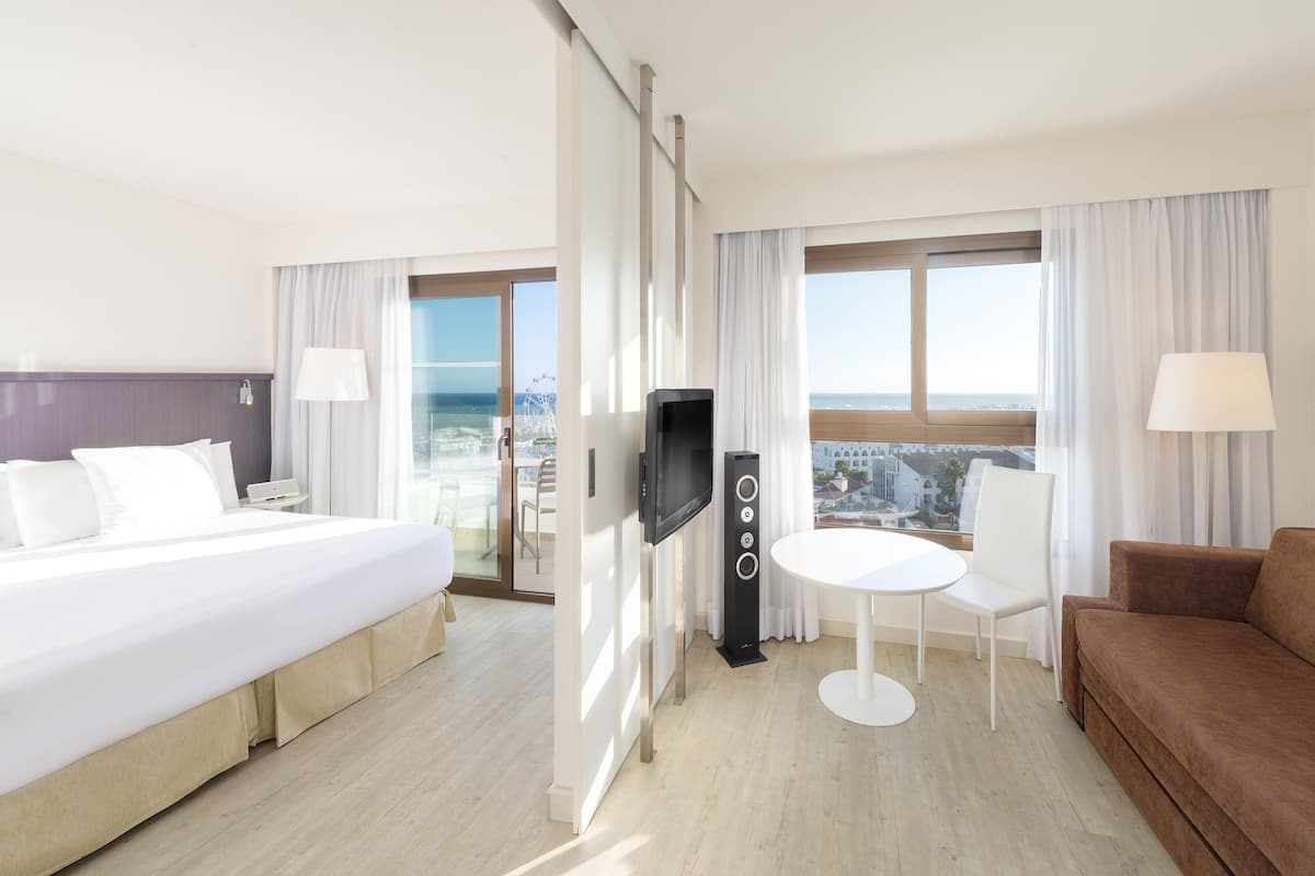 Quarto de hotel com cama, televisão, uma pequena mesa com cadeiras e um sofá.
