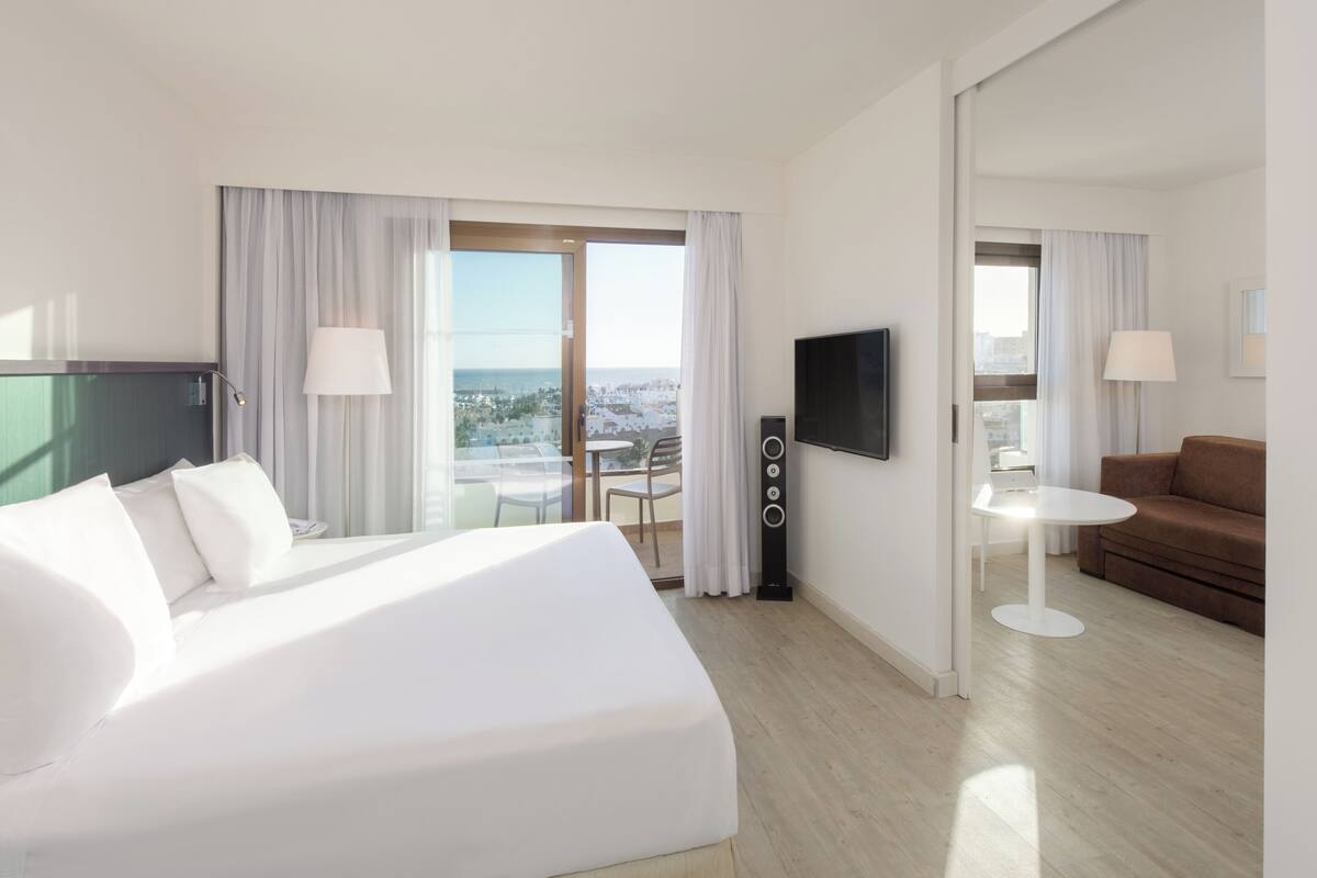 Quarto de hotel com cama, televisão, varanda com vista, sofá e uma pequena mesa.