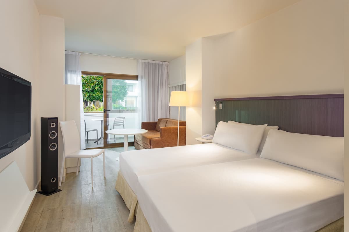 Quarto de hotel com cama grande, televisão, secretária e cadeira, e vista para o exterior.