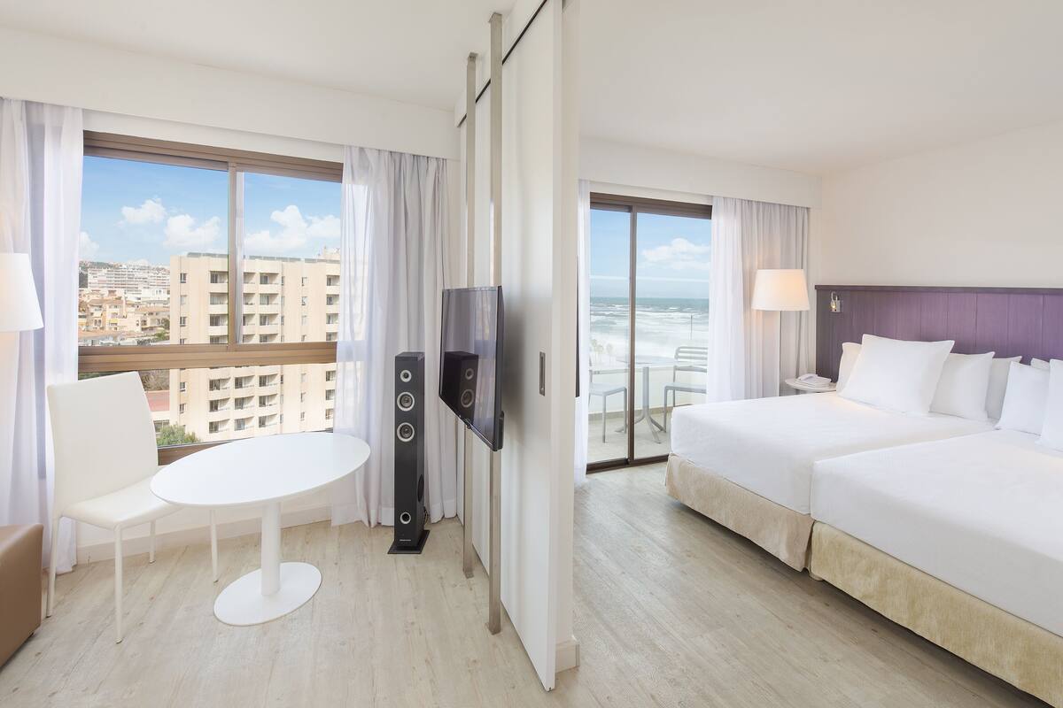 Quarto de hotel com varanda, televisão, cama, mesa e cadeira.