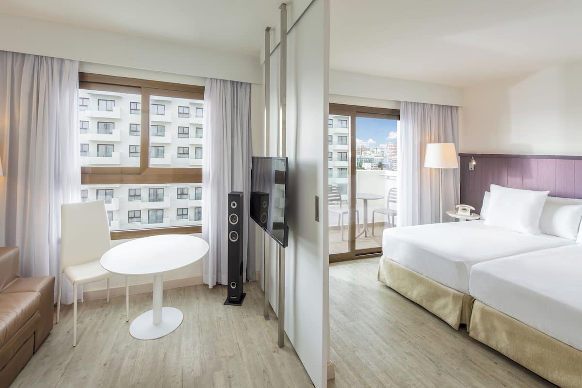 Quarto de hotel com cama, escrivaninha, cadeira, televisão e varanda com vista para edifícios.