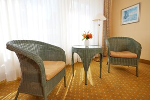 Quarto com duas cadeiras de vime, uma mesa de vidro pequena com um vaso de flores e um abajur.