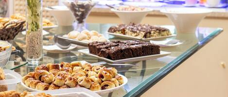 Uma mesa de buffet com diversos pães e sobremesas.