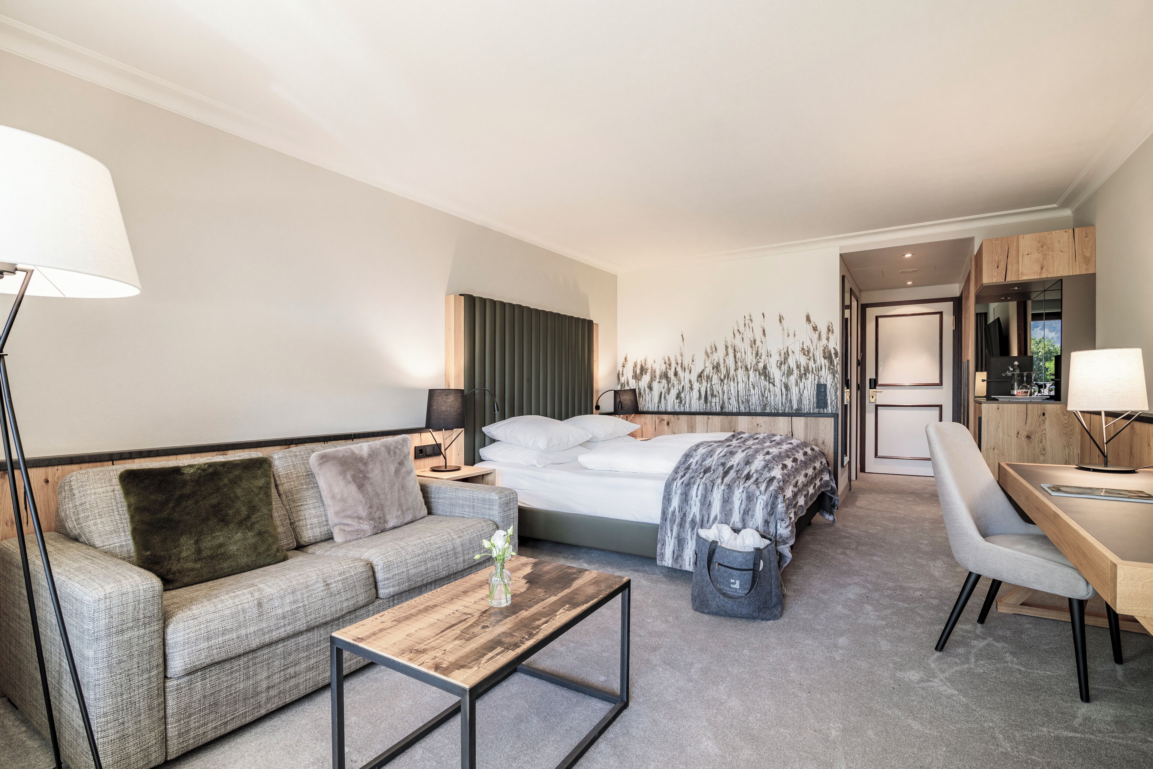 Quarto de hotel moderno com cama, sofá, escrivaninha e luminária.